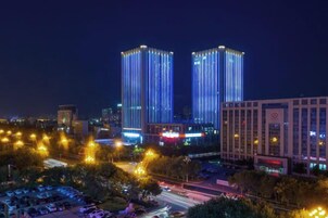 Paisagem urbana noturna com edifícios iluminados e uma área de estacionamento.