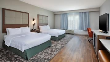 Quarto de hotel com duas camas, uma mesa, uma cadeira, televisão e janela com cortinas.