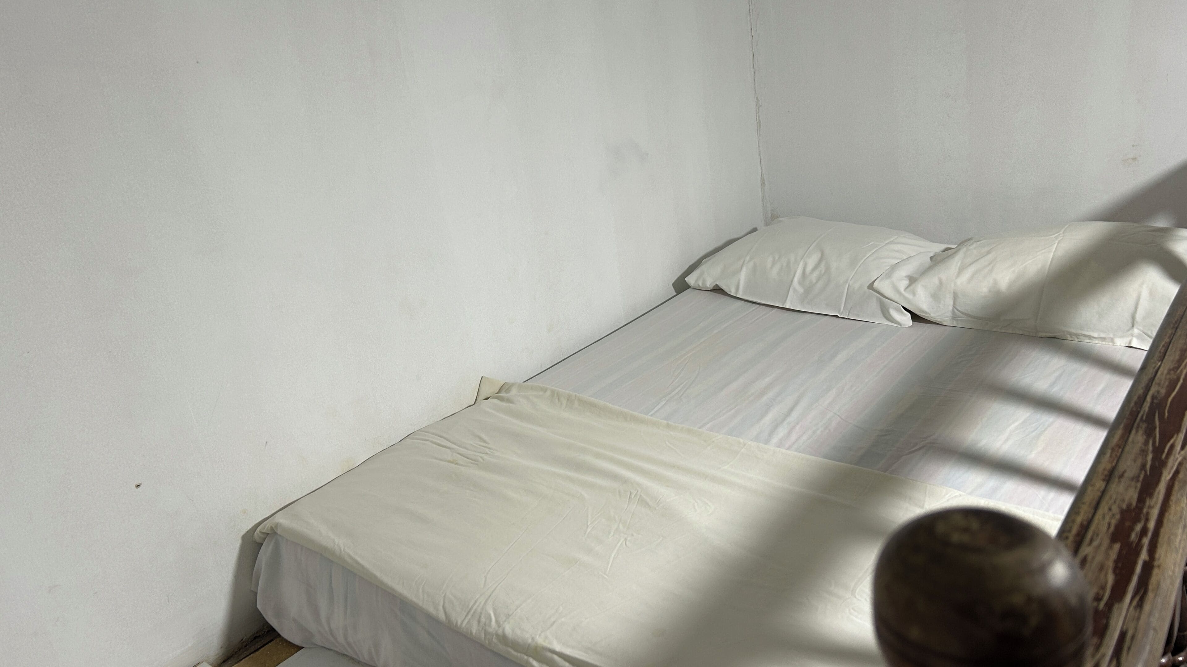 Quarto pequeno com uma cama de solteiro, roupa de cama branca e porta de madeira.