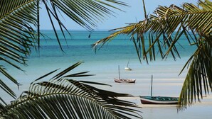 Uma praia com águas turquesa cristalinas, um barco pequeno e palmeiras.