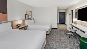 Quarto de hotel com duas camas, uma escrivaninha com cadeira, televisão e uma lixeira verde.