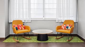 Um quarto com duas cadeiras de balanço, uma mesa redonda e um tapete verde.