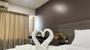 Quarto de hotel com uma cama, arranjo de toalhas em forma de cisne decorativo, um vaso com flores e um aparelho de ar condicionado.