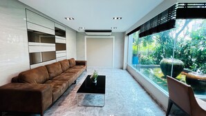 Uma sala de estar moderna com um sofá de couro marrom, uma mesa de centro preta e uma grande janela com vista para um jardim e uma fonte.