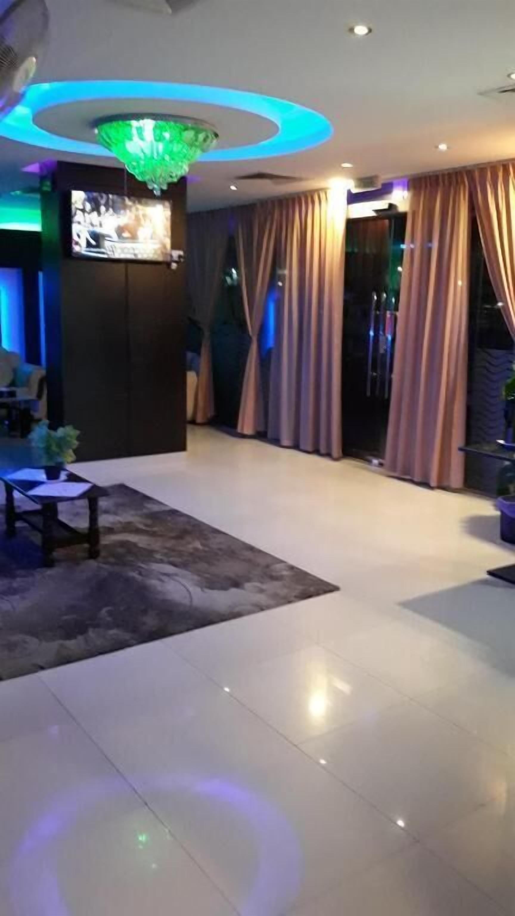 Um saguão de hotel com uma televisão de tela plana, uma área de estar com mesa e cadeiras, e uma grande janela com cortinas.