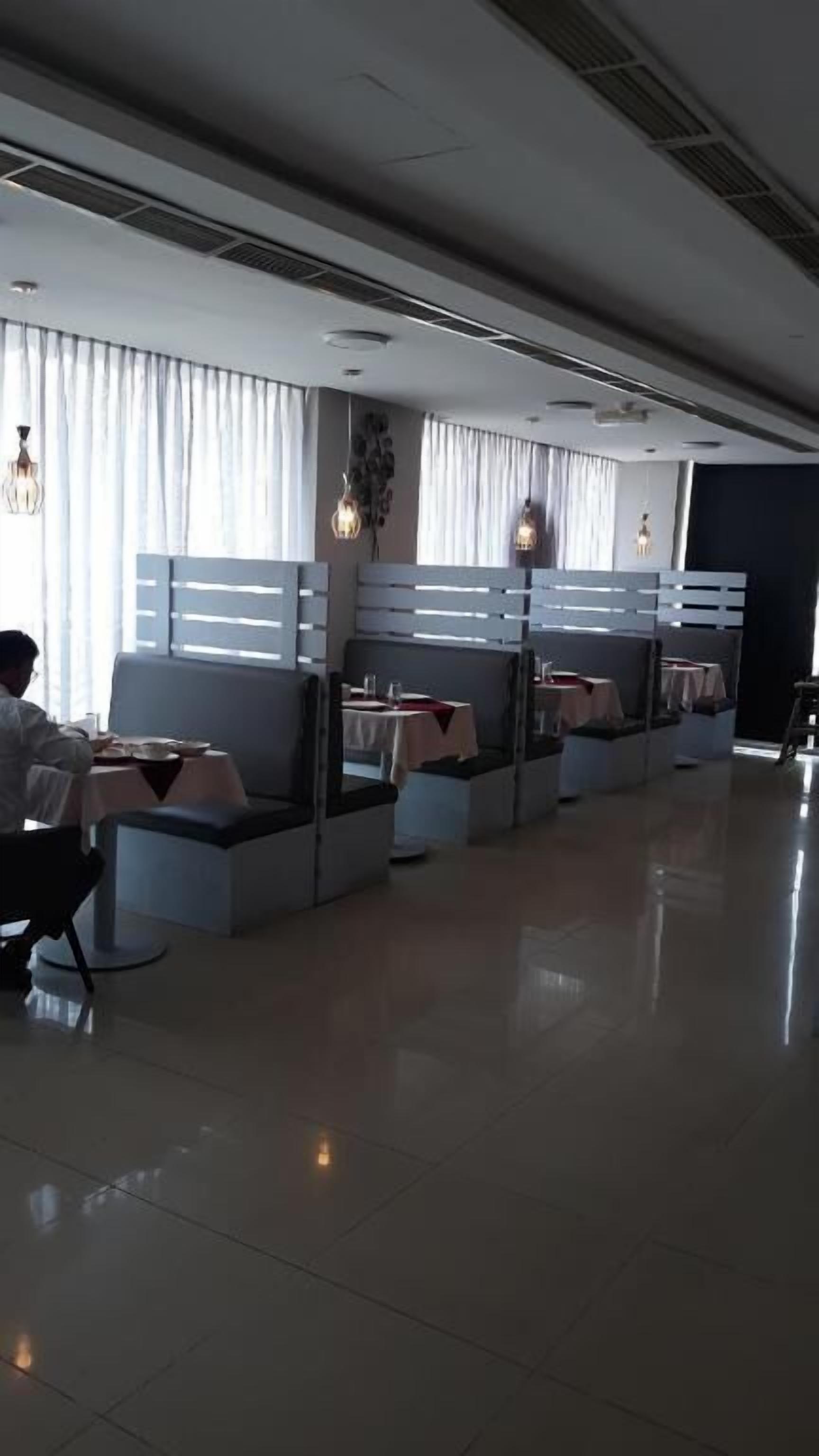Restaurante com assentos em camarote, mesas e uma pessoa sentada à mesa.