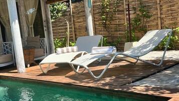 Uma área de piscina com espreguiçadeiras, um espaço de estar coberto e um deck de madeira.