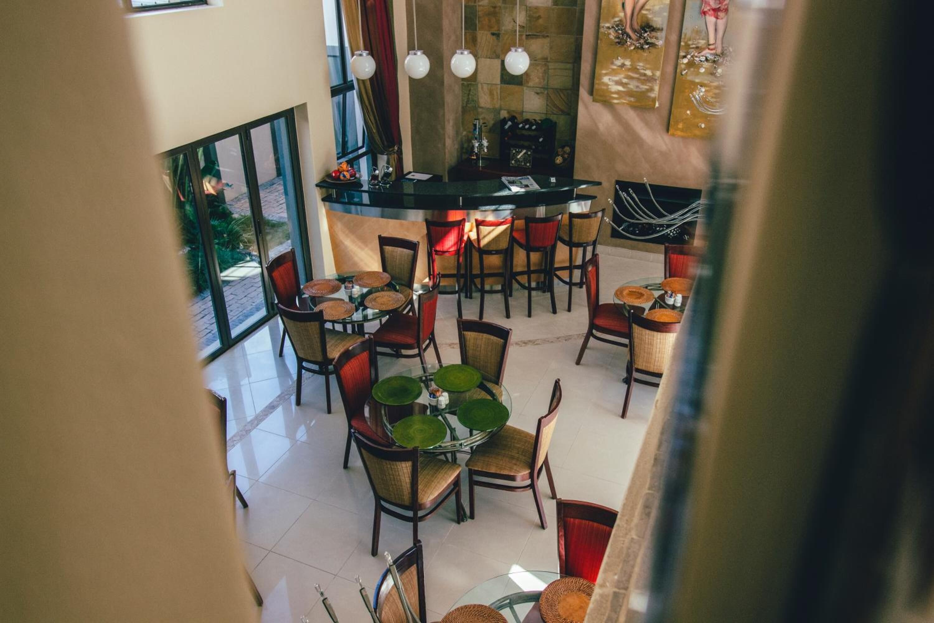 Um restaurante com mesas e cadeiras redondas, um espaço de bar e uma grande janela com vista para a rua.