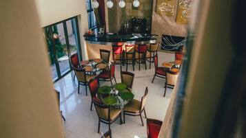 Um restaurante com mesas e cadeiras redondas, um espaço de bar e uma grande janela com vista para a rua.