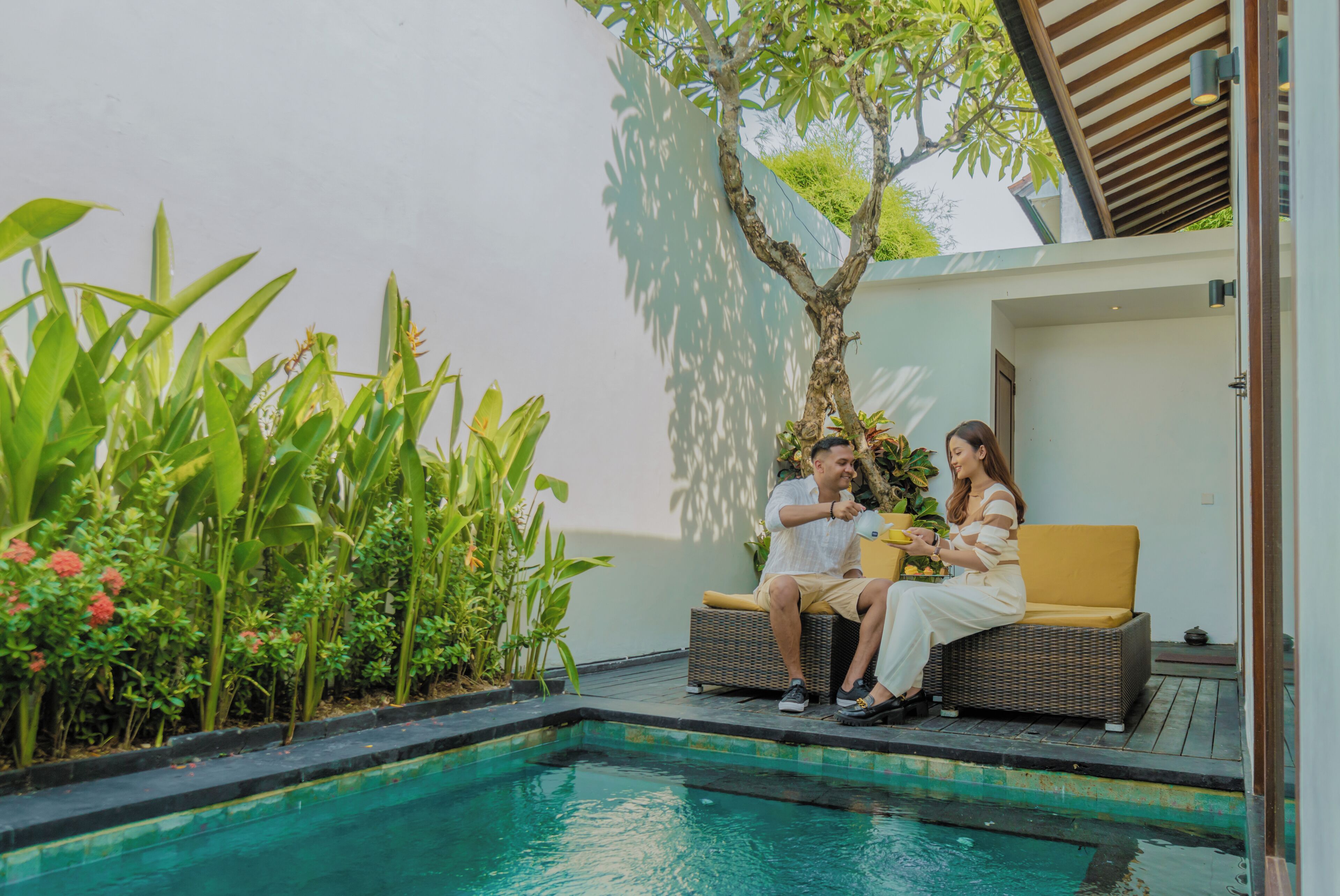 Uma área à beira da piscina com mobiliário de vime e vegetação exuberante.