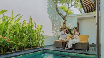 Uma área à beira da piscina com mobiliário de vime e vegetação exuberante.