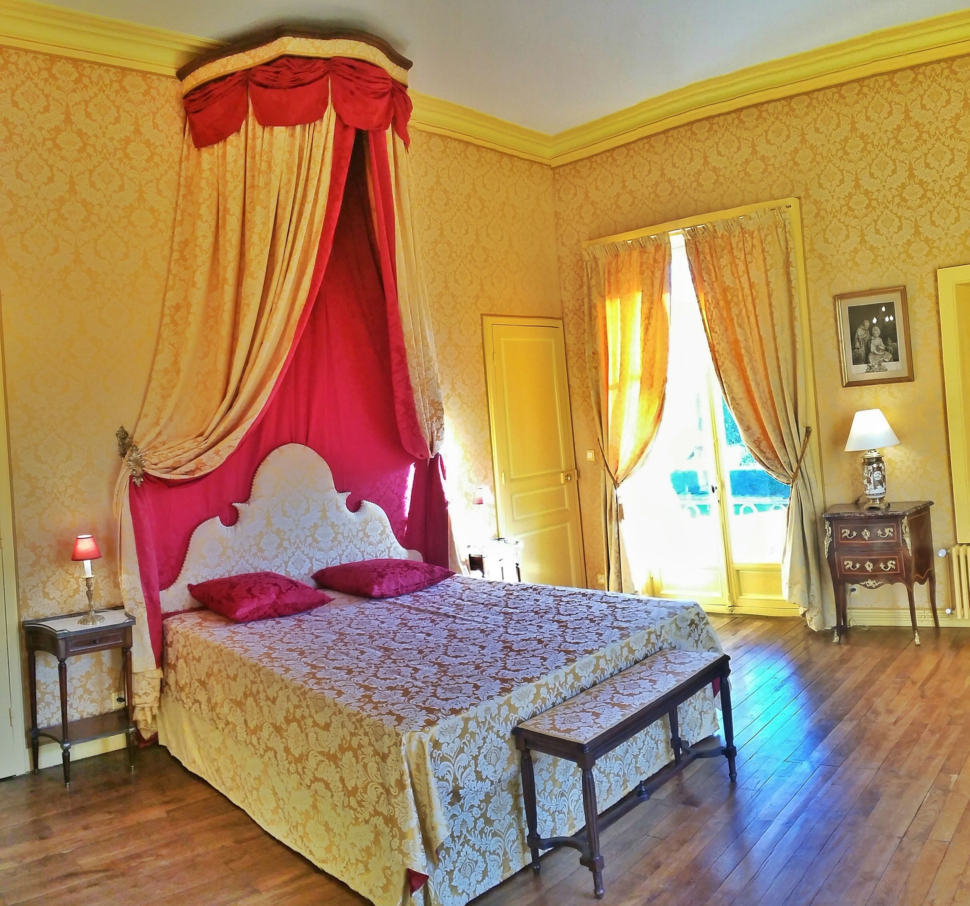 Quarto com cama de dossel, mesa de cabeceira com abajur e um quadro na parede.