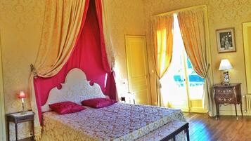 Quarto com cama de dossel, mesa de cabeceira com abajur e um quadro na parede.