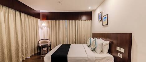 Quarto de hotel com uma cama grande, mesa de cabeceira, uma cadeira e um abajur.