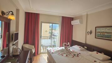 Quarto de hotel com cama, escrivaninha, cadeira, televisão e varanda com cortinas vermelhas.