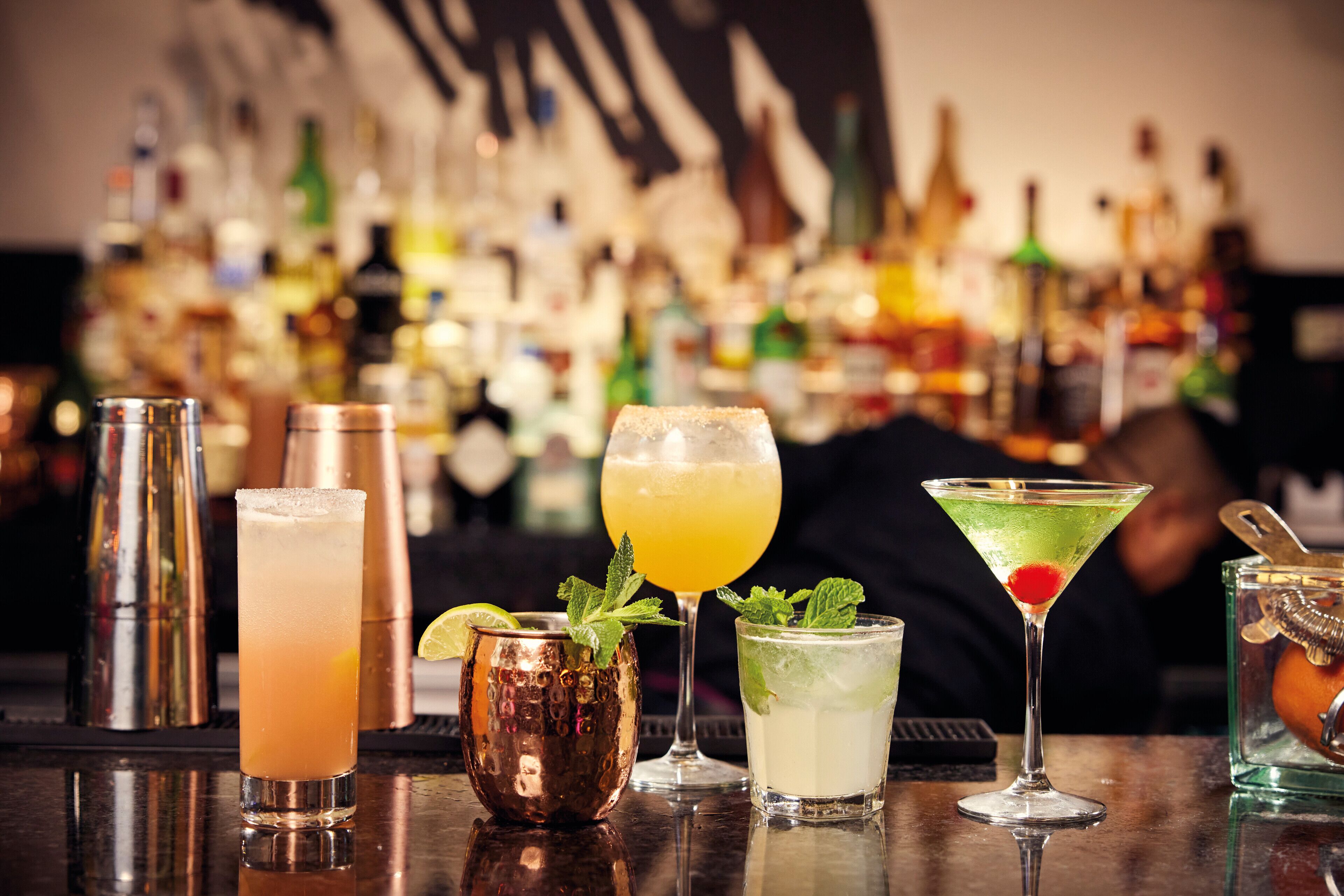 Um bar com diversas bebidas, incluindo um copo alto, um copo baixo e um copo de martini.