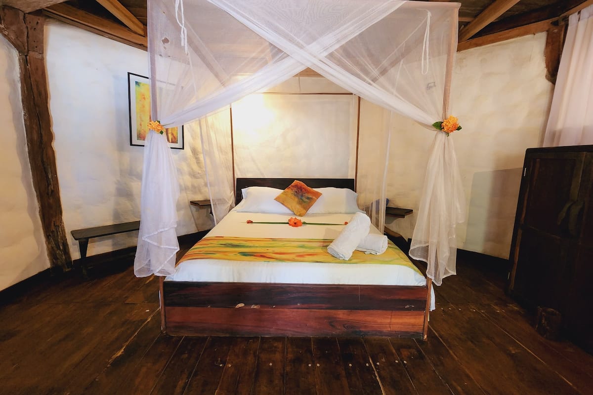 Uma cama com dossel, piso de madeira e um quadro pendurado na parede.