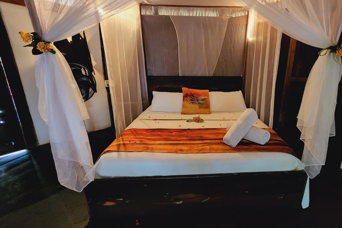 Cama com cabeceira de madeira, roupa de cama branca e almofada decorativa.