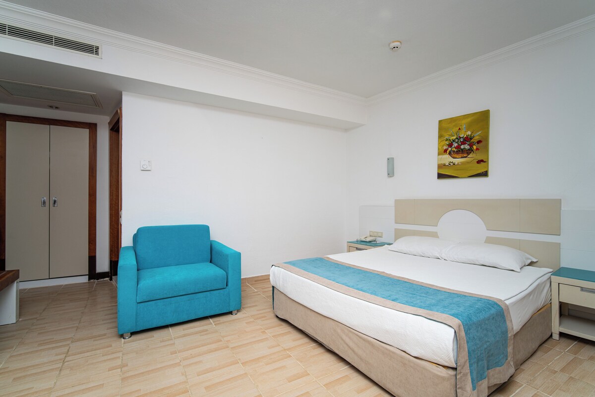 Um quarto com uma cama, uma cadeira azul, uma mesa de cabeceira e um quadro pendurado na parede.