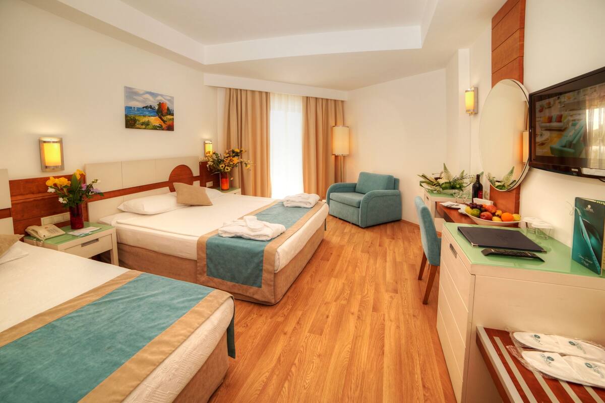 Quarto de hotel com duas camas, uma escrivaninha com um laptop, uma cadeira, uma televisão e uma janela com cortinas.