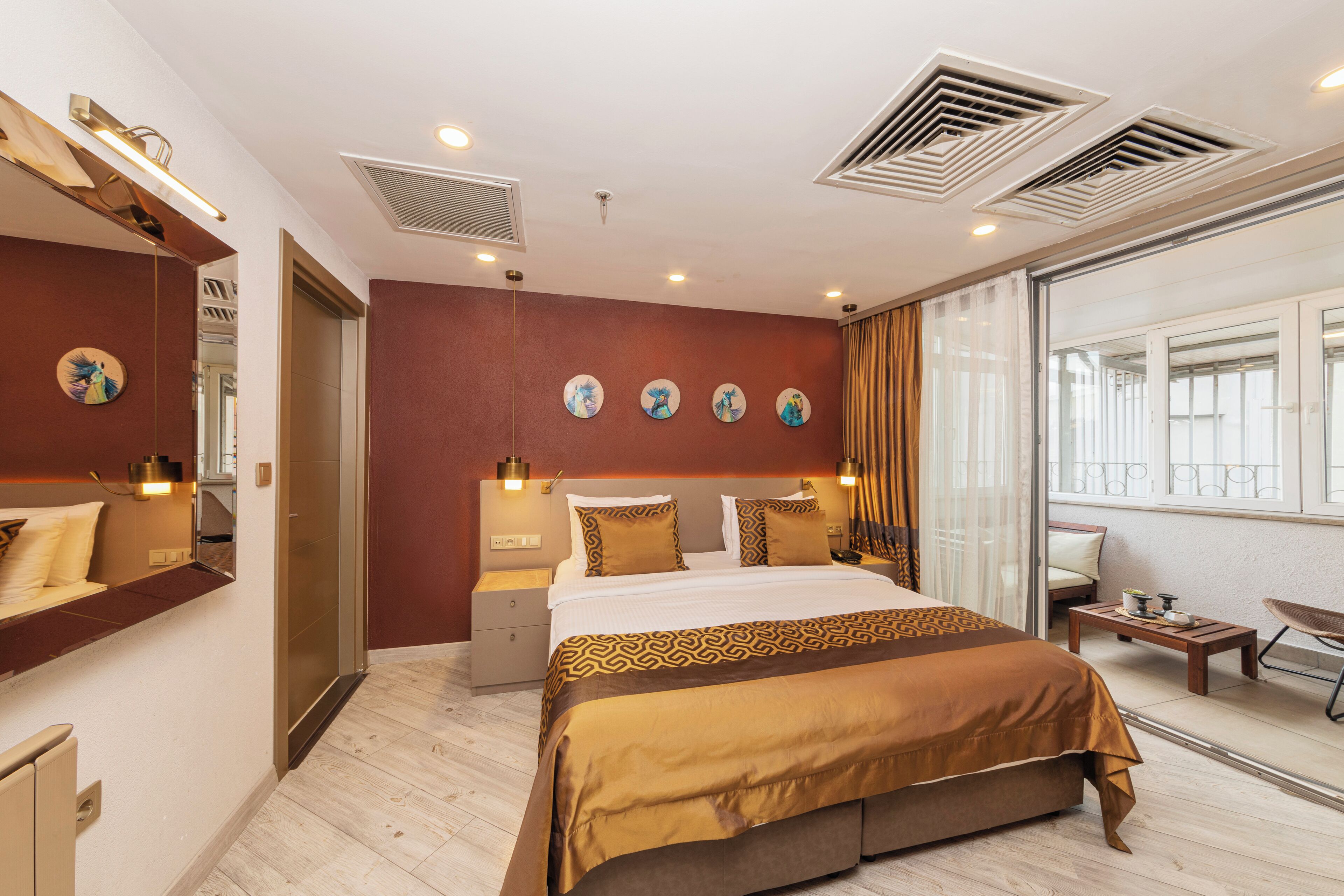 Quarto de hotel com cama, mesas de cabeceira, espelho, janela com cortinas e um pequeno espaço de estar.