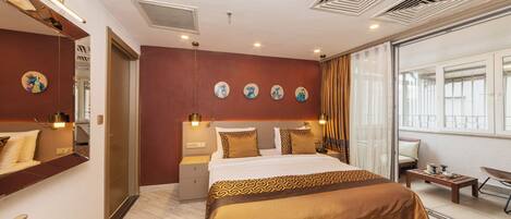 Quarto de hotel com cama, mesas de cabeceira, espelho, janela com cortinas e um pequeno espaço de estar.
