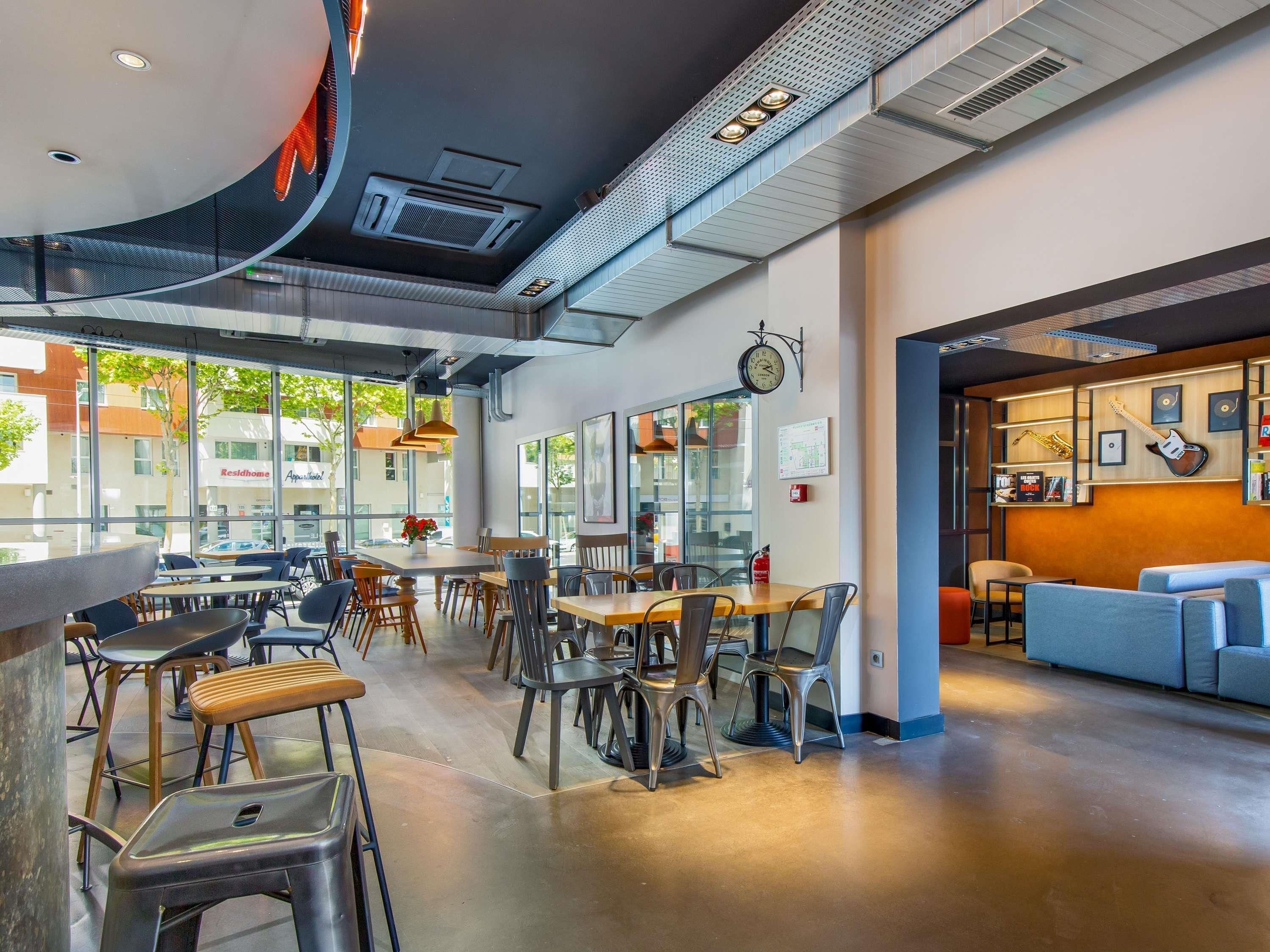 Interior moderno de café com mesas, cadeiras, um relógio e vista para o exterior.