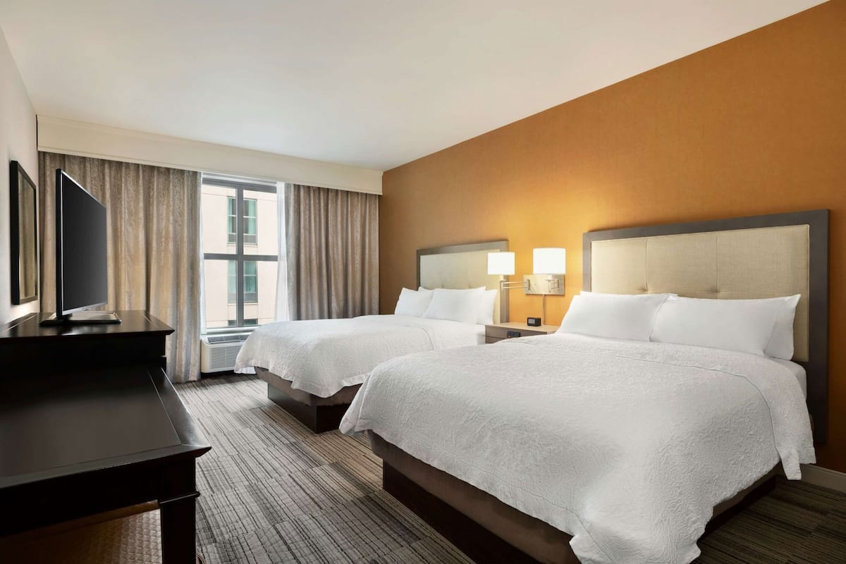 Quarto de hotel com duas camas, televisão e escrivaninha.