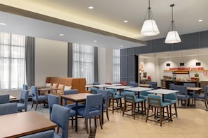 Uma sala de jantar de hotel com mesas, cadeiras, um sofá e um balcão de café da manhã.