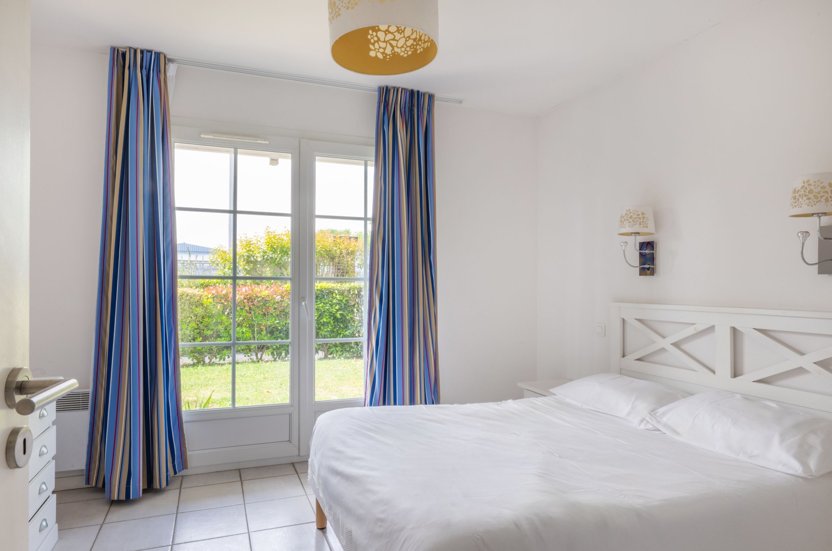 Quarto com cama, cortinas, janela e porta.