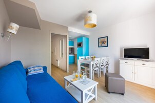 Uma sala de estar moderna com um sofá azul, uma mesa de centro branca e uma TV sobre um móvel branco.