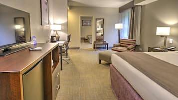 Quarto de hotel com cama, escrivaninha com computador, cadeira, luminária e televisão.