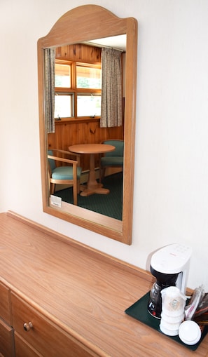 Uma cômoda de madeira com um espelho em cima, refletindo um quarto com uma mesa e cadeiras de madeira.