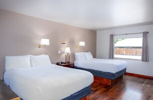 Quarto de hotel com duas camas, piso de madeira e janela com cortinas.