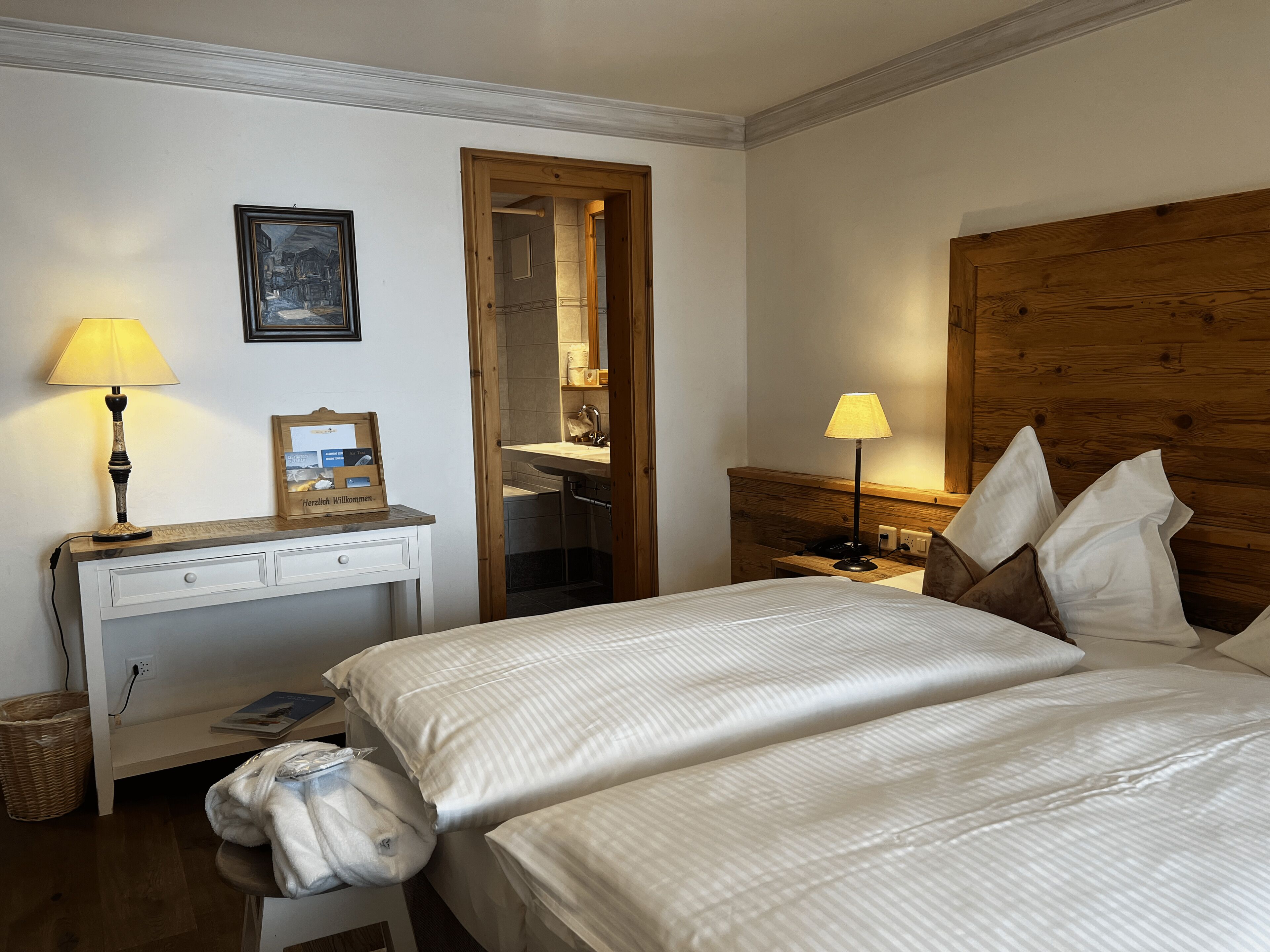 Quarto de hotel com duas camas, uma escrivaninha, um espelho e cabeceira de madeira.