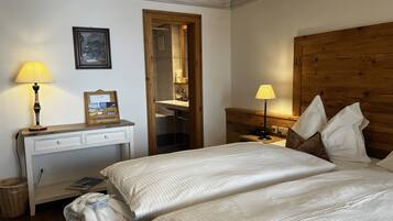 Quarto de hotel com duas camas, uma escrivaninha, um espelho e cabeceira de madeira.