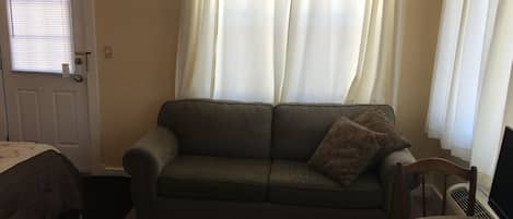 Uma sala de estar com um sofá, uma televisão e um controle remoto sobre uma mesinha.