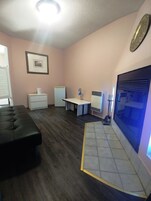 Quarto com sofá de couro preto, uma mesinha branca com um vaso, armário branco, aquecedor e um espelho grande.