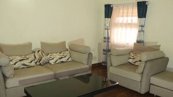 Uma sala de estar com sofá, mesa de centro de vidro e janela com cortinas.