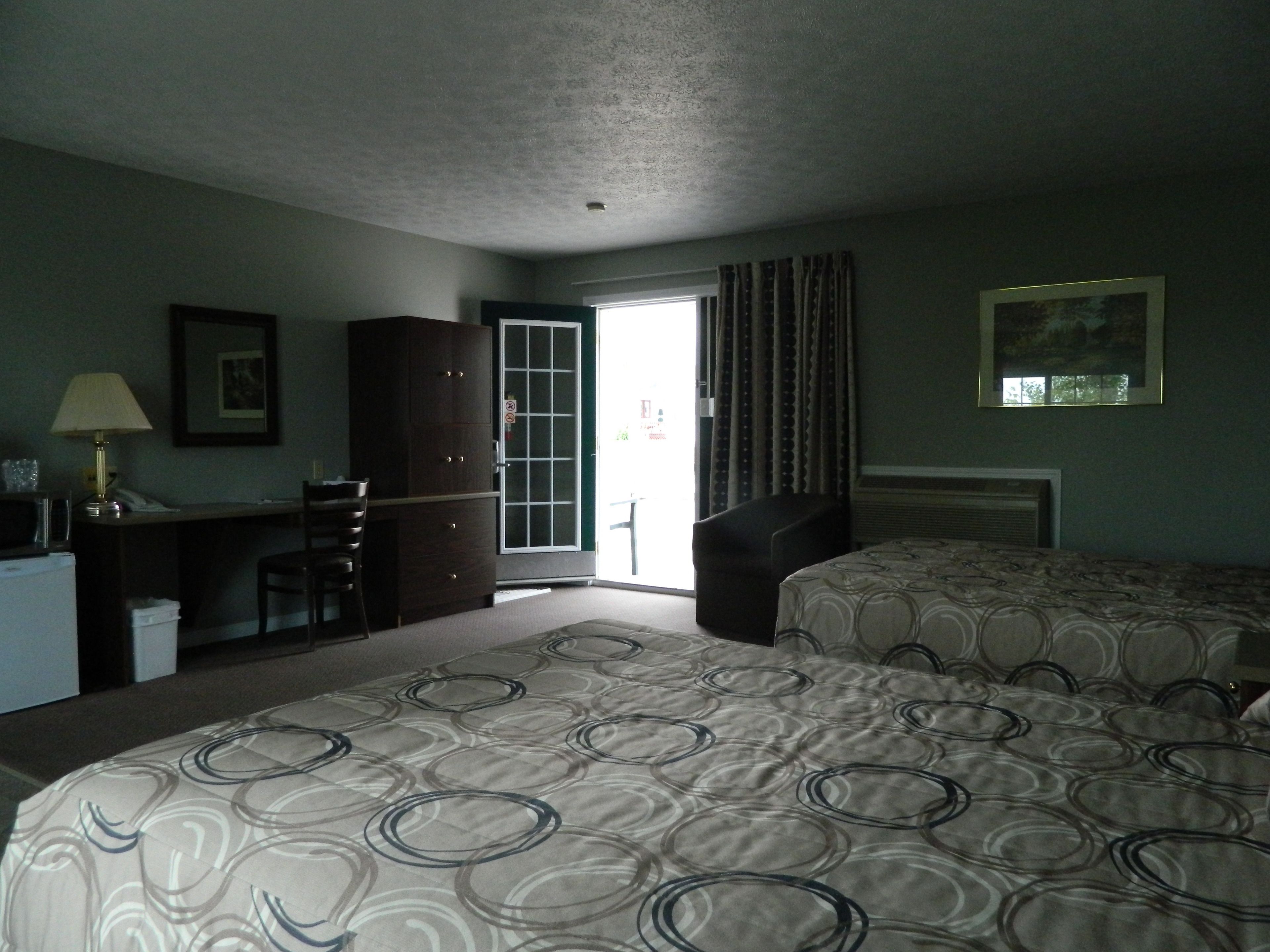 Quarto de hotel com duas camas, uma escrivaninha com cadeira, um guarda-roupa e uma porta para o exterior.