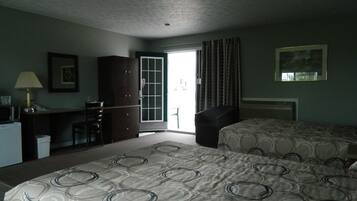 Quarto de hotel com duas camas, uma escrivaninha com cadeira, um guarda-roupa e uma porta para o exterior.