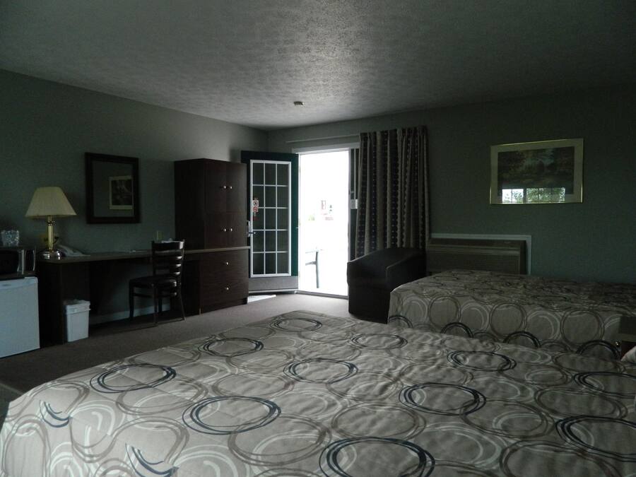 Quarto de hotel com duas camas, uma escrivaninha com cadeira, um guarda-roupa e uma porta para o exterior.