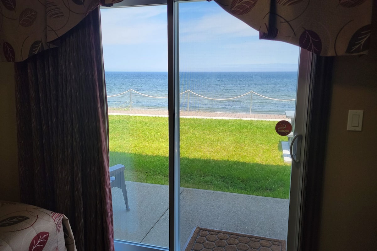 Quarto com porta de vidro deslizante que dá para uma varanda com vista para o mar e uma área gramada.