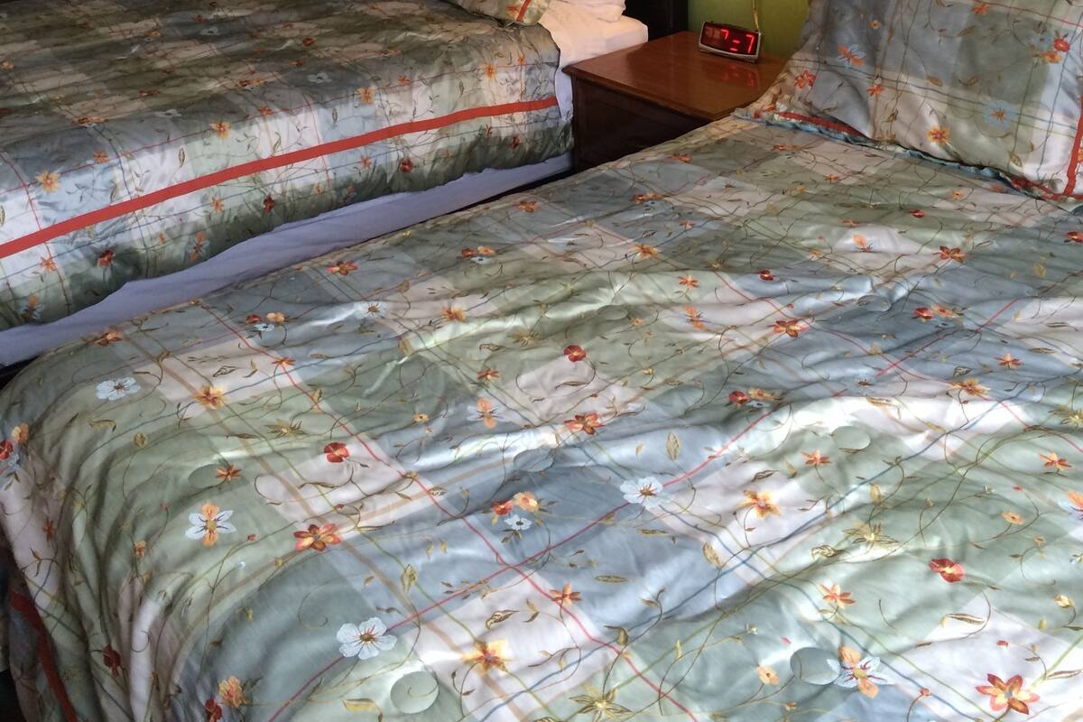 Quarto com duas camas, cada uma com roupa de cama estampada com flores, uma mesa de cabeceira com abajur e um relógio de parede.