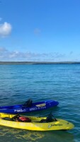 Dois caiaques, um azul e um amarelo, em águas calmas sob um céu claro e terra ao longe.