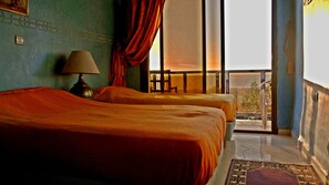 Quarto de hotel com duas camas, uma luminária, janela com cortinas e vista para o exterior.