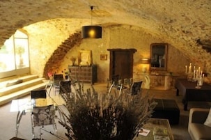 Interior rústico com teto de pedra, lareira e área de estar com uma mesa de centro e cadeiras.