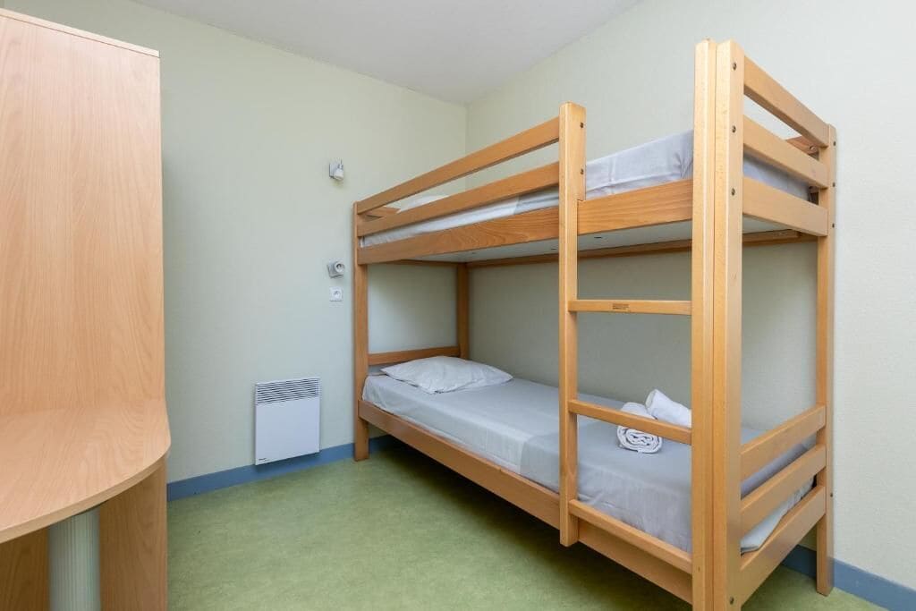 Quarto com beliche, escrivaninha de madeira e radiador.