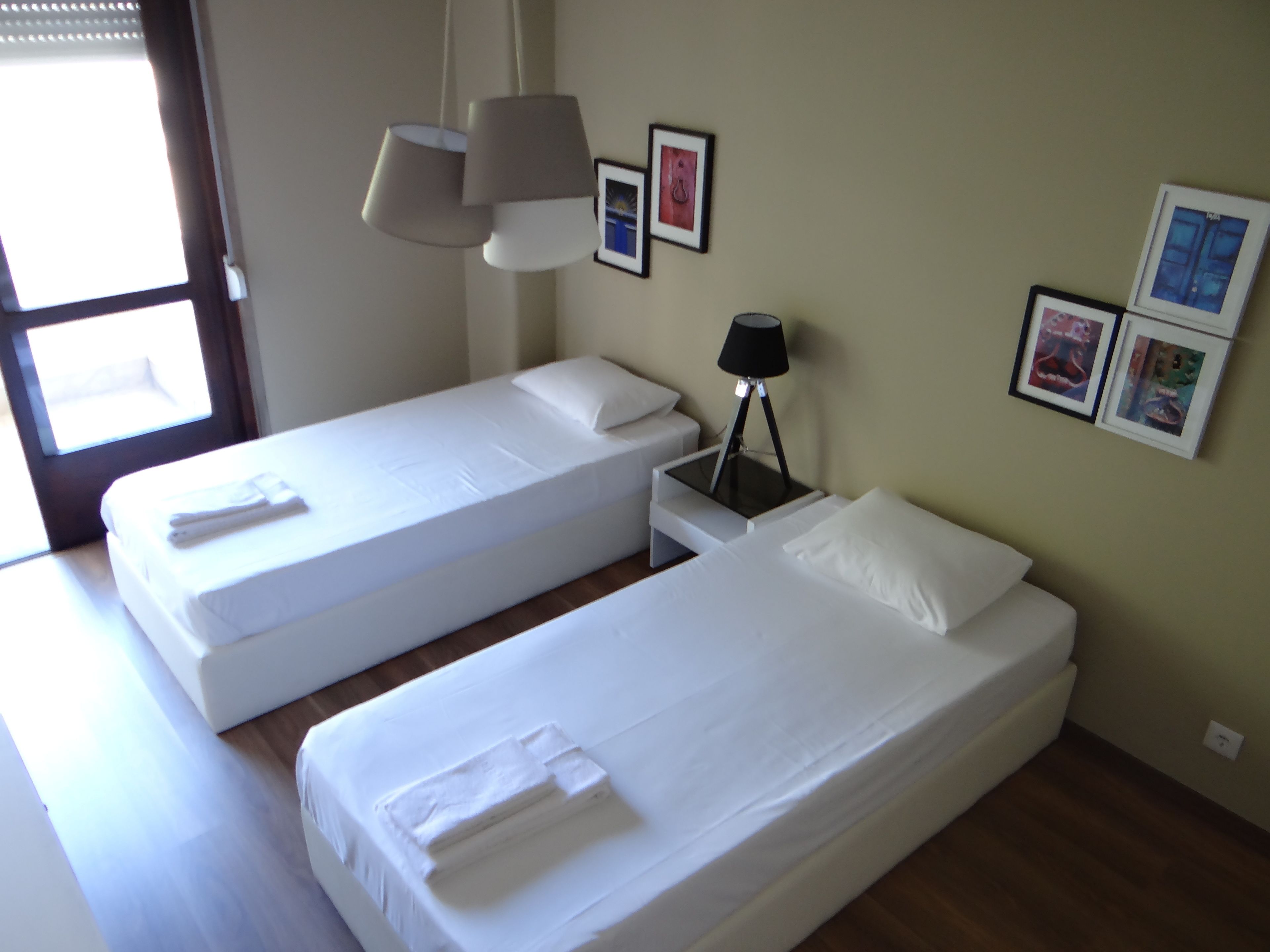 Quarto com duas camas de solteiro, uma mesa de cabeceira com luminária e quadros nas paredes.