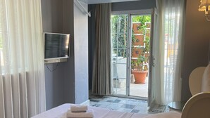 Quarto de hotel com cama, TV fixada na parede, ar condicionado, telefone e vista da área externa por uma porta de vidro.